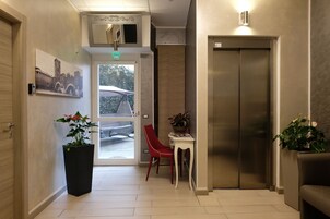 Um hall moderno com uma porta grande, uma cadeira vermelha, uma mesinha e um elevador.
