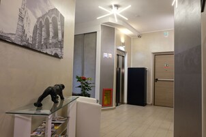 Um corredor com uma mesa de vidro, uma escultura, um quadro e um elevador.