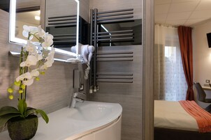 Casa de banho moderna com lavatório branco, espelho, porta-toalhas e uma orquídea em vaso.