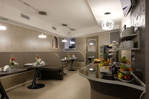Um restaurante moderno com cabines, mesas redondas e um balcão central com frutas e pão.