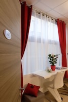 Quarto moderno com porta de madeira, cortinas vermelhas, escrivaninha branca com planta em vaso e almofada vermelha em uma cadeira.
