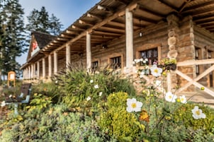 Uma cabana rústica de madeira com varanda, cercada por um jardim cheio de flores.