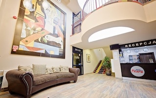 Um saguão de hotel com uma grande pintura abstrata, um balcão de recepção, uma escadaria e um sofá.