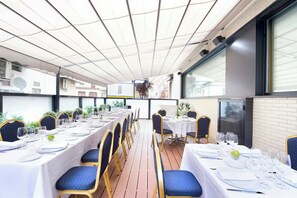 Restaurante com várias mesas preparadas para refeições, design moderno com teto em azulejos e vista para a paisagem urbana.