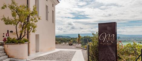 Entrada de hotel com um caminho de pedra que leva a um edifício, uma placa de identificação e vista para o campo.