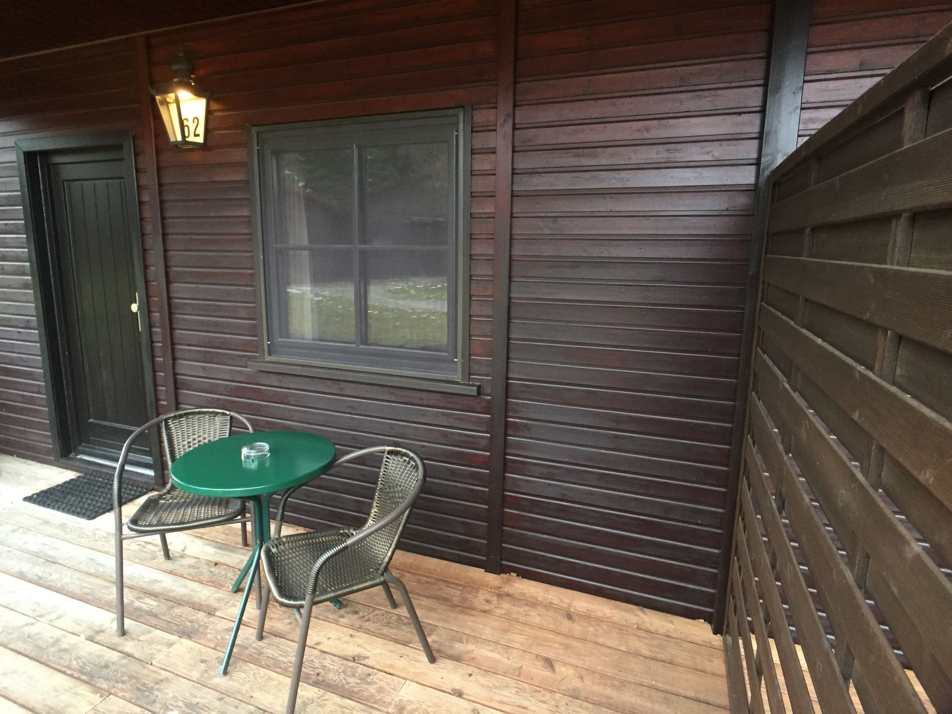 Fachada de madeira com uma mesa verde e duas cadeiras de vime em um deck de madeira.