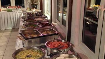 Buffet montado com diversos alimentos e área de refeições com vista para o céu noturno.