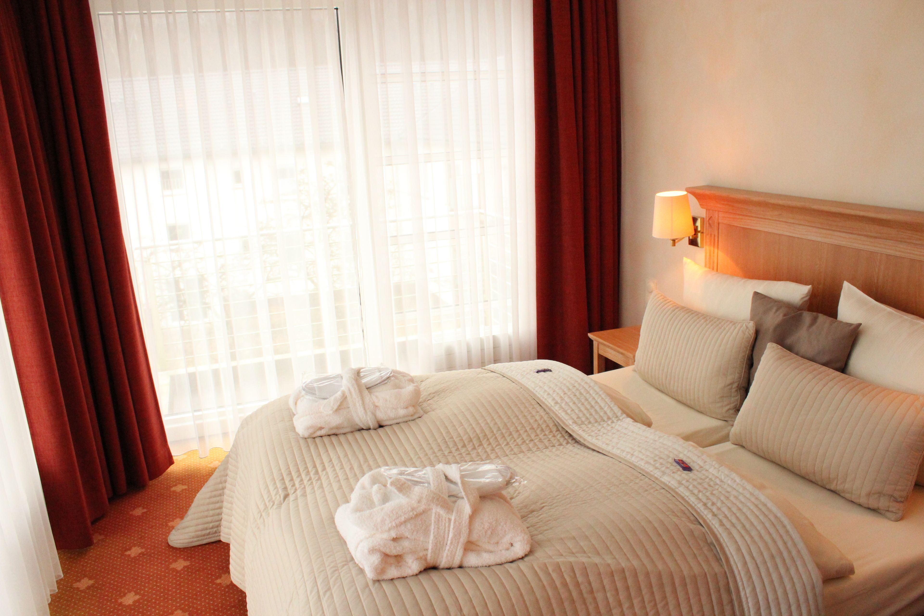 Quarto de hotel com uma cama grande, mesa de cabeceira, abajur e janela com cortinas.