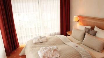 Quarto de hotel com uma cama grande, mesa de cabeceira, abajur e janela com cortinas.