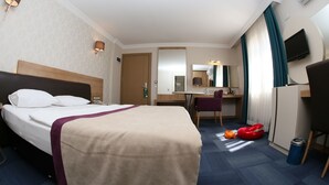 Quarto de hotel com cama, escrivaninha, cadeira e televisão.