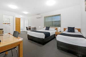 Quarto de hotel com duas camas, uma escrivaninha e um chuveiro.