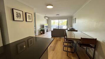 Cozinha moderna com bancada preta e piso de madeira, área de jantar com mesa e cadeiras, e vista para o exterior através de uma porta de correr.