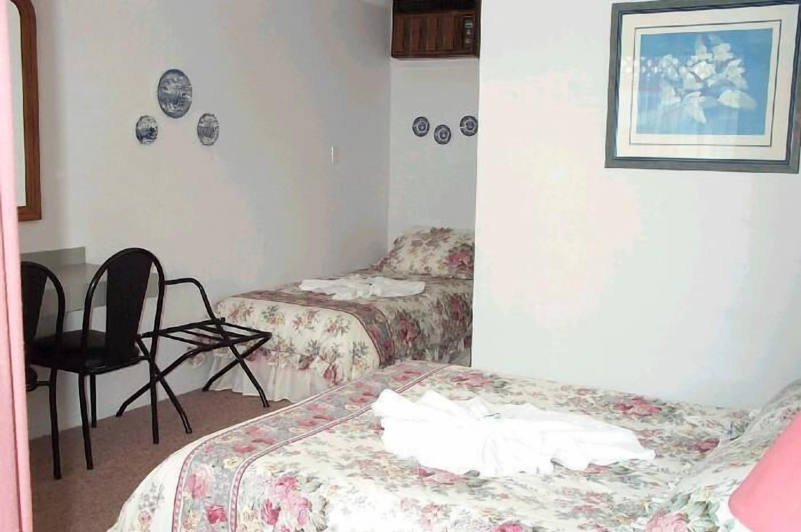 Quarto com duas camas, uma cadeira e decorações nas paredes.