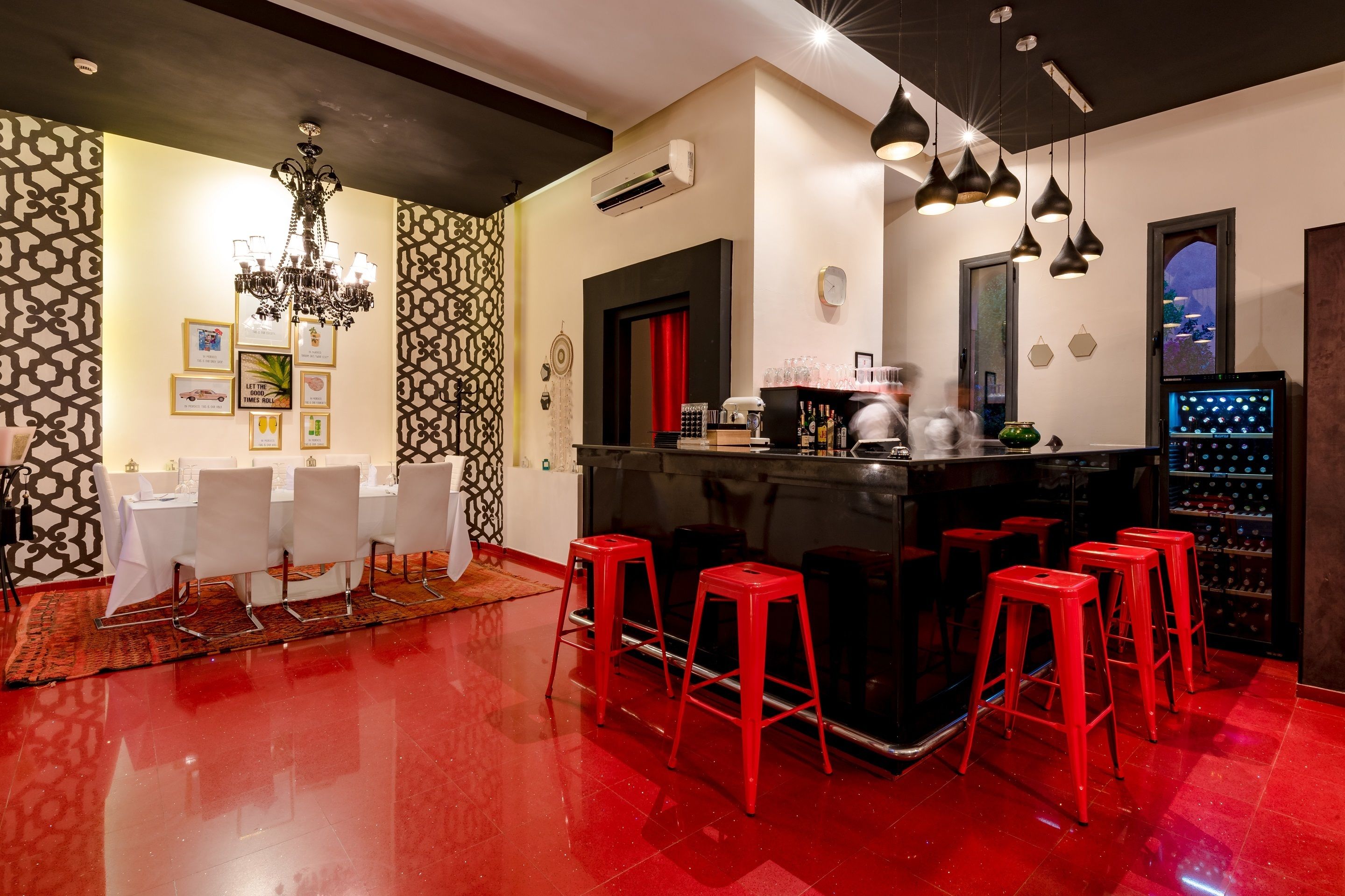 Uma área de bar com banquetas vermelhas, um balcão preto e uma cortina vermelha.