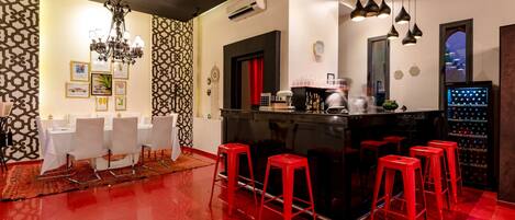 Uma área de bar com banquetas vermelhas, um balcão preto e uma cortina vermelha.