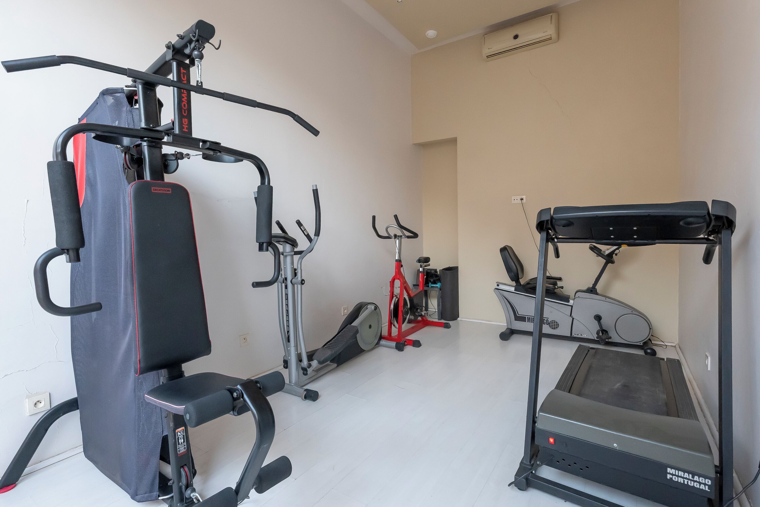 Academia com máquinas de cardio, um banco de musculação e esteira.