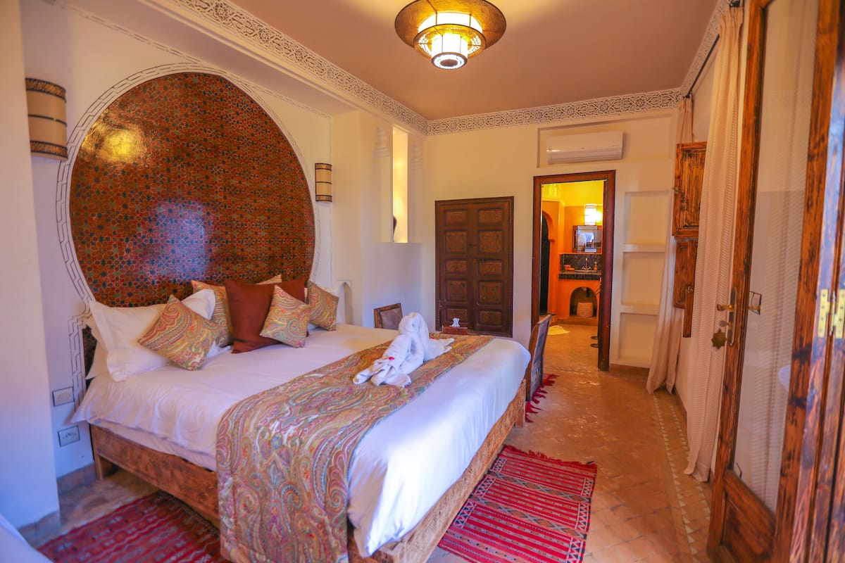 Um quarto espaçoso com uma cama grande, cabeceira elaborada e um tapete vermelho estampado.