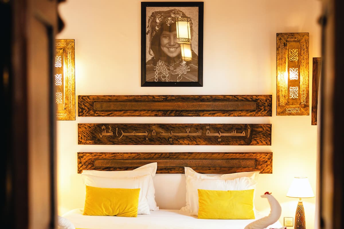 Um quarto com cama, mesa de cabeceira, abajur e um quadro na parede.