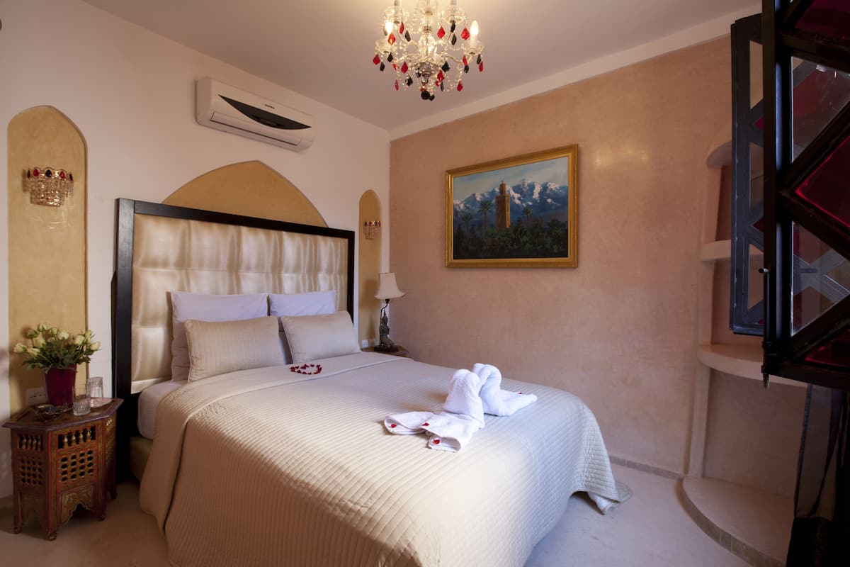 Quarto de hotel com uma cama grande, um candelabro, um quadro na parede e uma escadaria.