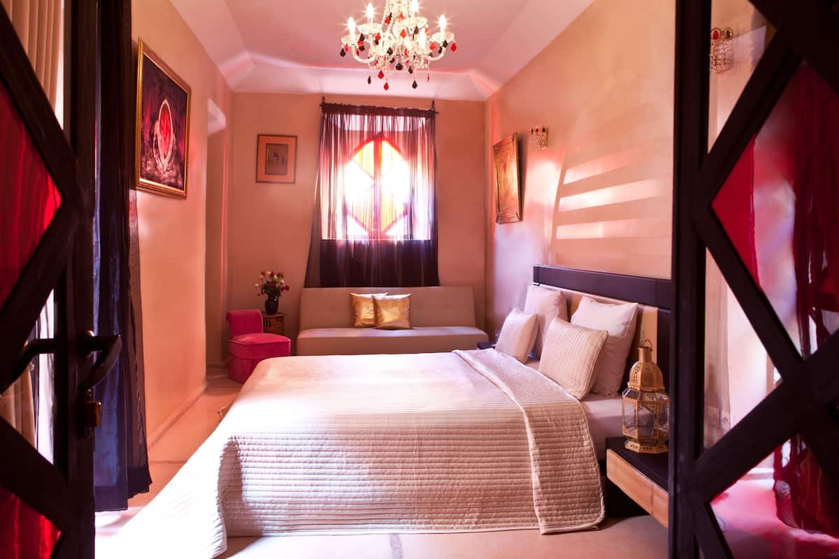 Quarto com cama grande, sofá, lustre e janela com cortinas.