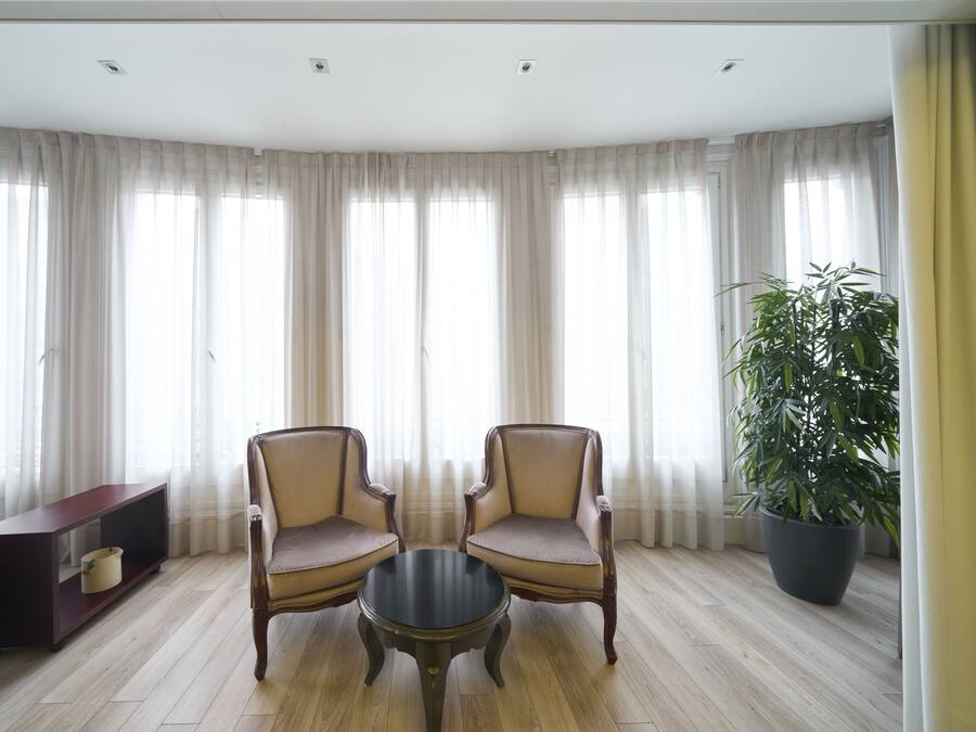Um quarto com duas poltronas, uma mesinha redonda, um aparador de madeira escura e uma grande planta em vaso.