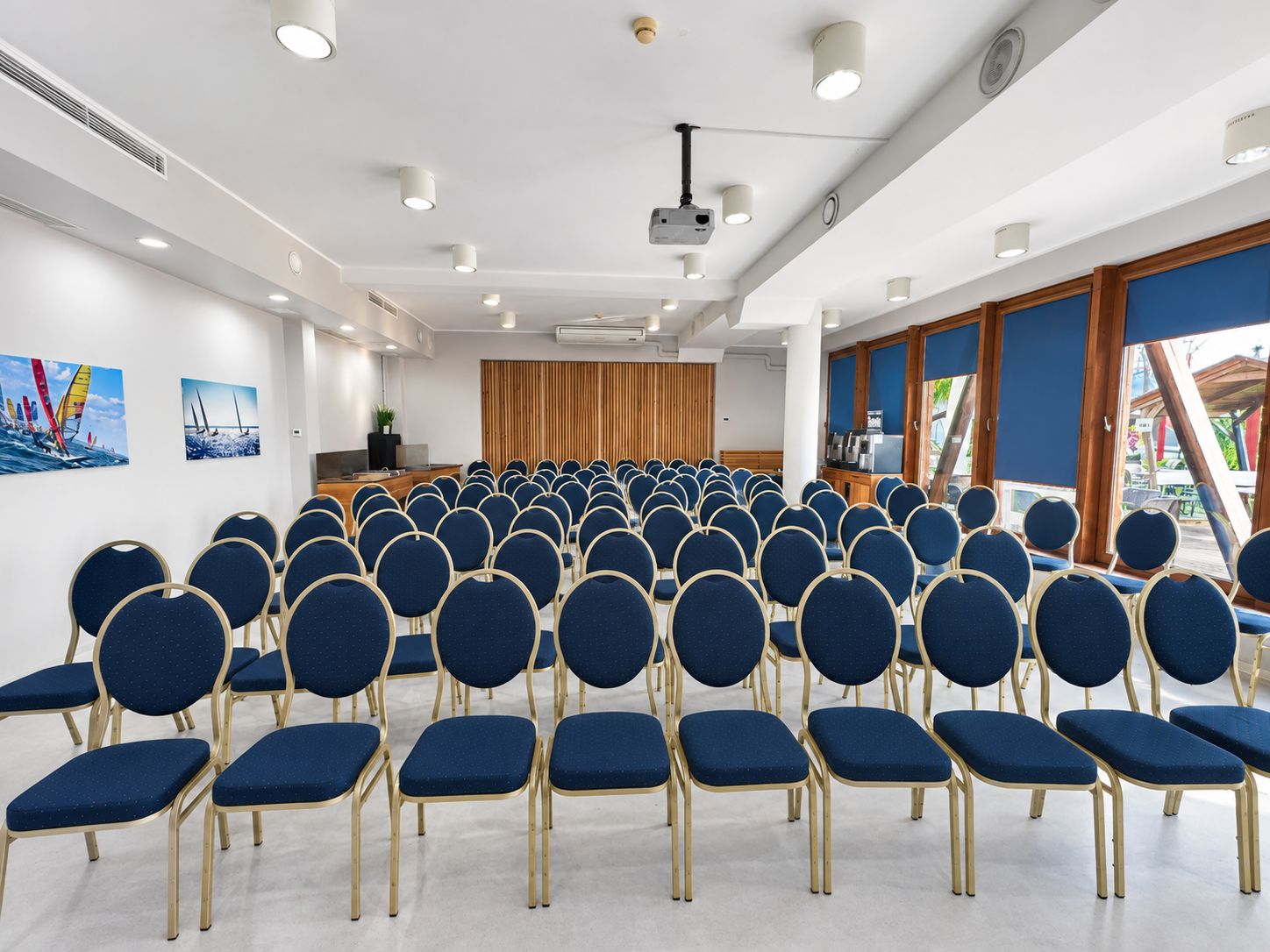 Uma sala de conferências com fileiras de cadeiras, um púlpito e um projetor.