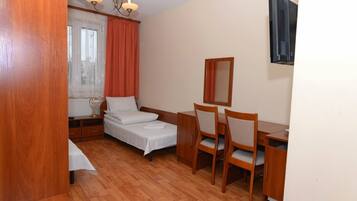 Quarto com cama, mesa de cabeceira, abajur, escrivaninha de madeira, cadeiras e espelho.