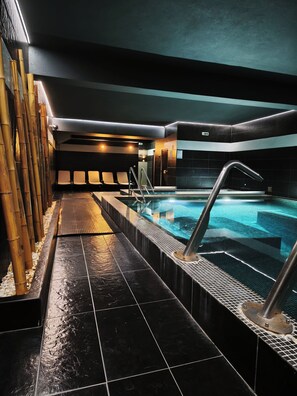 Piscina interior moderna com água cristalina, cercada por revestimento de azulejos pretos e detalhes em bambu.