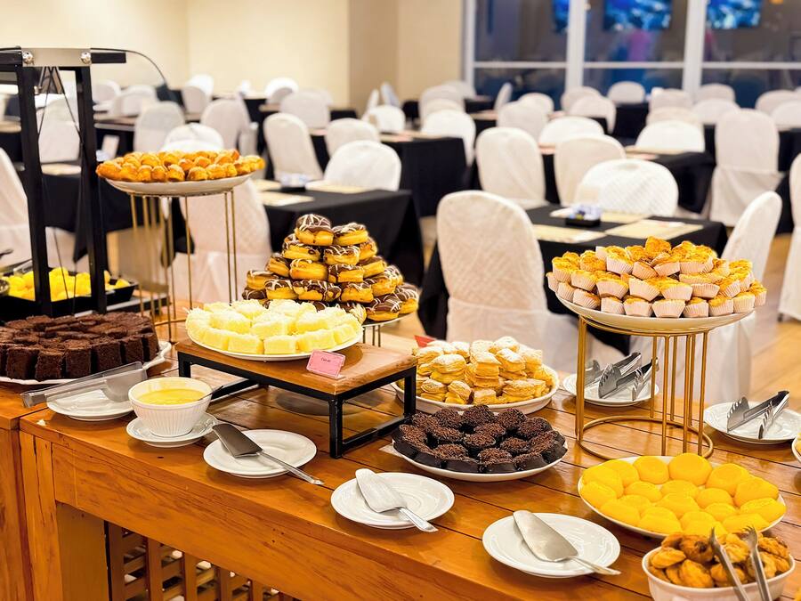 Uma mesa de buffet com diversos doces e pastelaria, incluindo bolos, donuts e biscoitos.