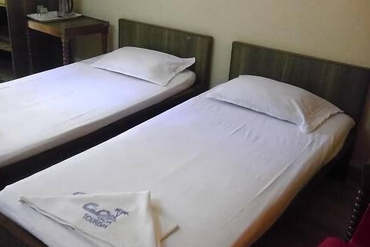 Duas camas de solteiro com lençóis e almofadas brancas, uma cabeceira de madeira e uma pequena mesa com um chaleira.