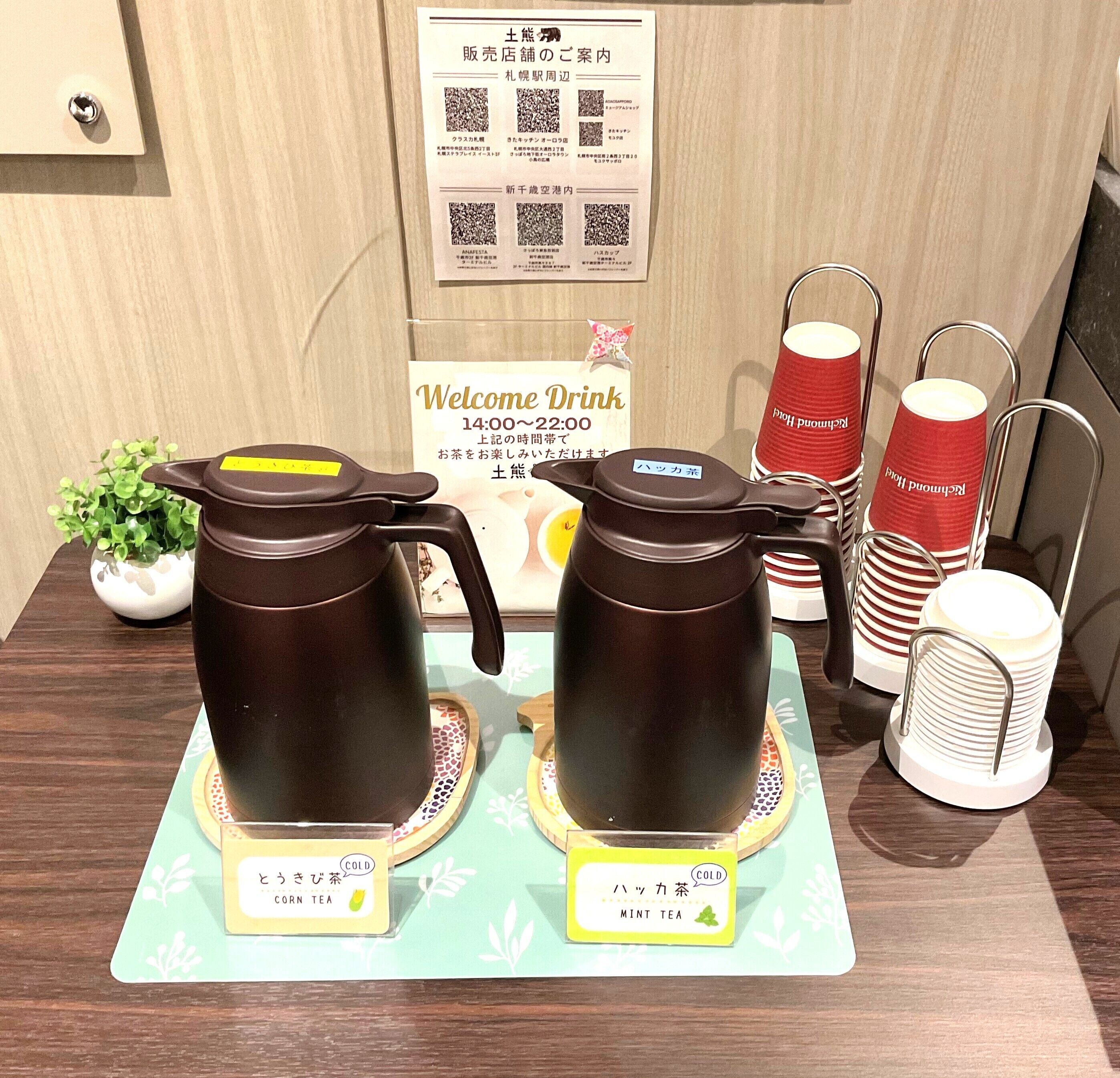 Uma estação de café com duas máquinas de café, um aviso para bebida de boas-vindas e um menu com código QR.