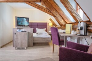 Quarto aconchegante com uma cama, escrivaninha, cadeira, televisão e teto de madeira.