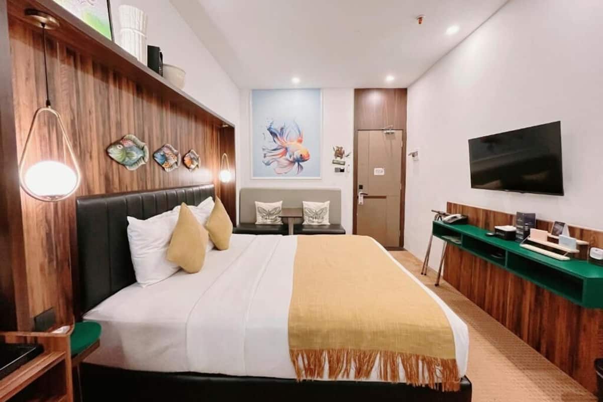 Quarto de hotel com uma cama grande, uma escrivaninha com televisão de tela plana, cabeceira de madeira e um quadro na parede.