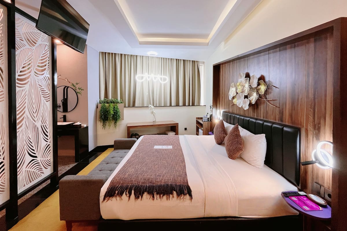 Quarto de hotel moderno com uma cama grande, uma escrivaninha, uma cadeira, uma TV e uma parede decorativa.