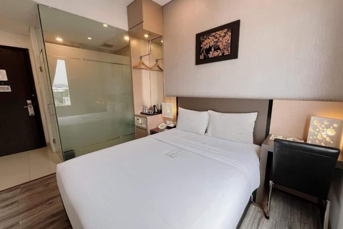 Quarto de hotel com uma cama grande, mesa de cabeceira, espelho e uma obra de arte pendurada na parede.