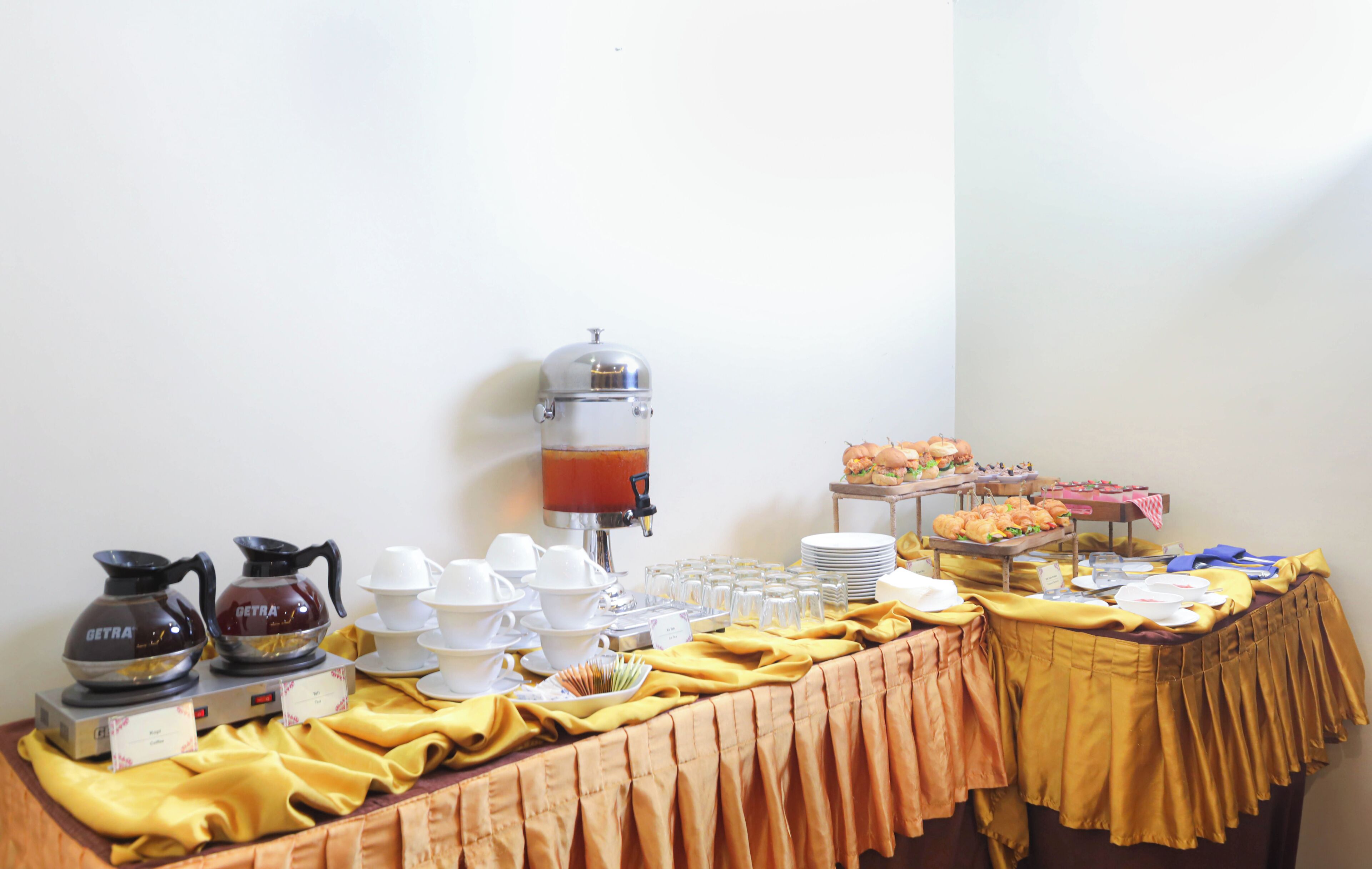 Disposição de buffet com máquinas de café, xícaras e diversos tipos de alimentos em uma mesa.
