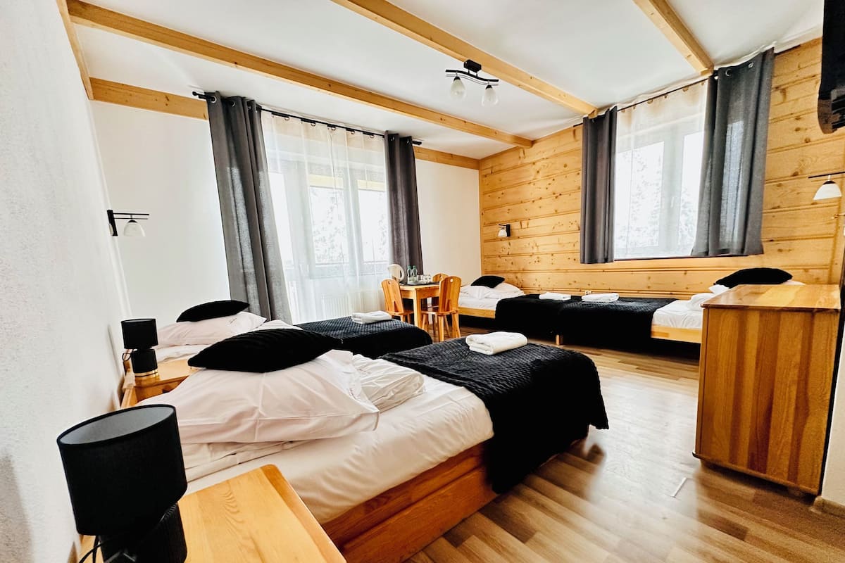 Quarto de hotel com duas camas, uma escrivaninha de madeira, uma cadeira, uma mesinha e um abajur.