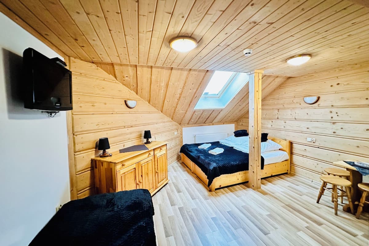 Quarto de cabana de madeira com duas camas, uma escrivaninha e uma TV.