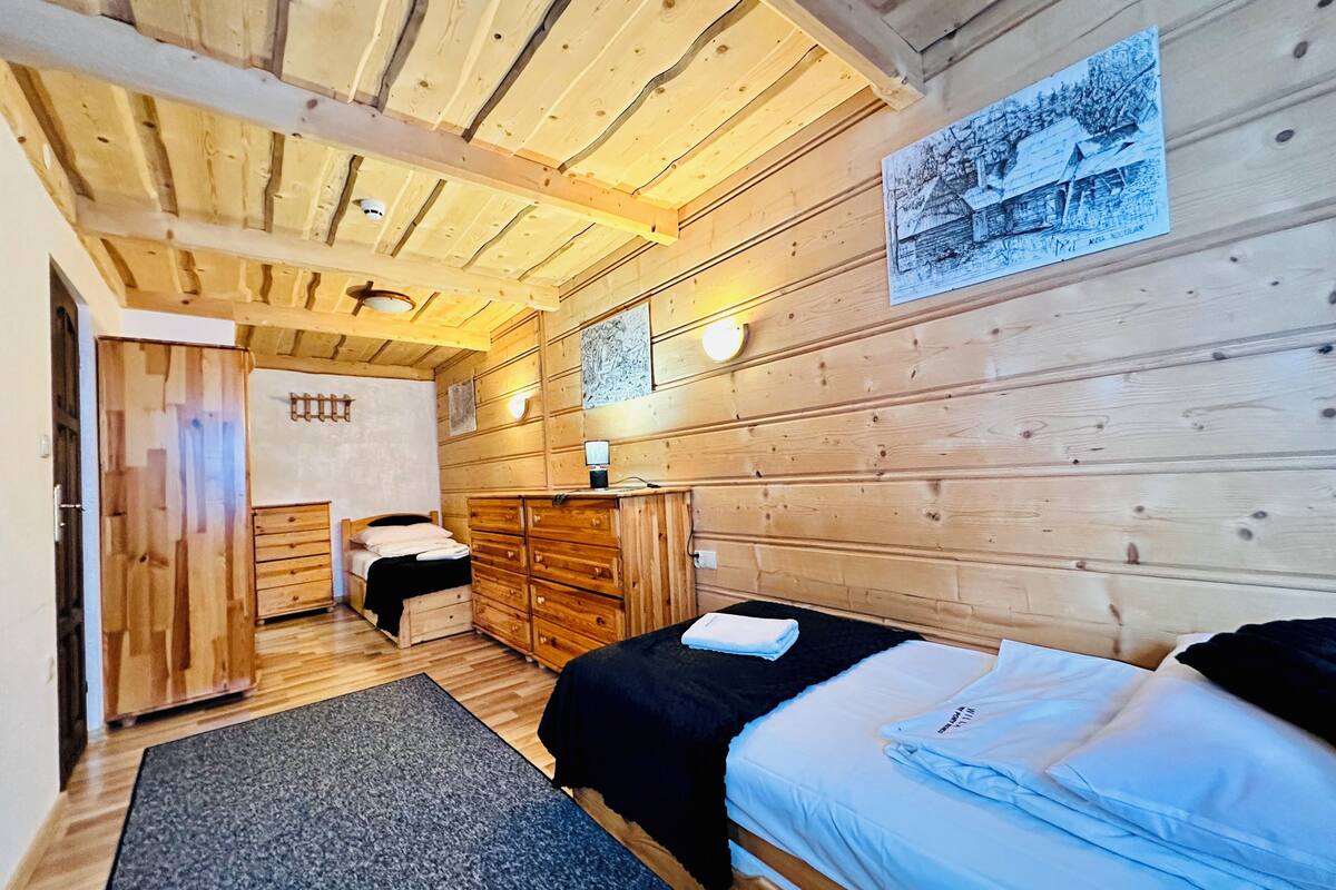 Quarto de cabana de madeira com duas camas, uma cômoda e uma pequena escrivaninha.