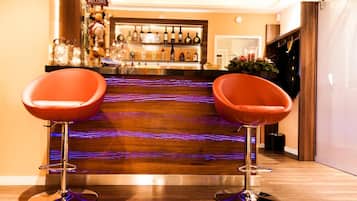 Uma área de bar com dois banquetas laranjas, piso de madeira e uma parede de garrafas de vinho.