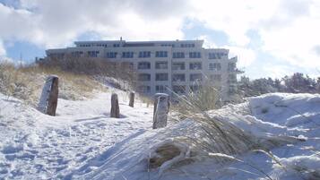 Um caminho coberto de neve que leva a um edifício com vários andares, telhado plano e muitas janelas.