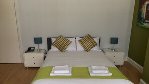 Cama bem arrumada com duas almofadas, duas mesas de cabeceira com abajures e um edredom verde.