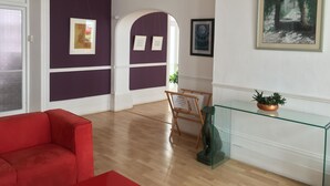 Um quarto com um sofá vermelho, uma mesa de vidro com uma planta e quadros nas paredes.