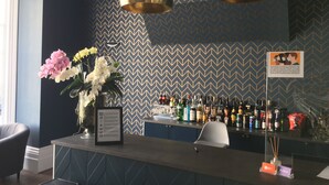 Uma área de bar com parede em padrão azul e dourado estilo Chevron, um menu emoldurado e diversas garrafas de bebidas.