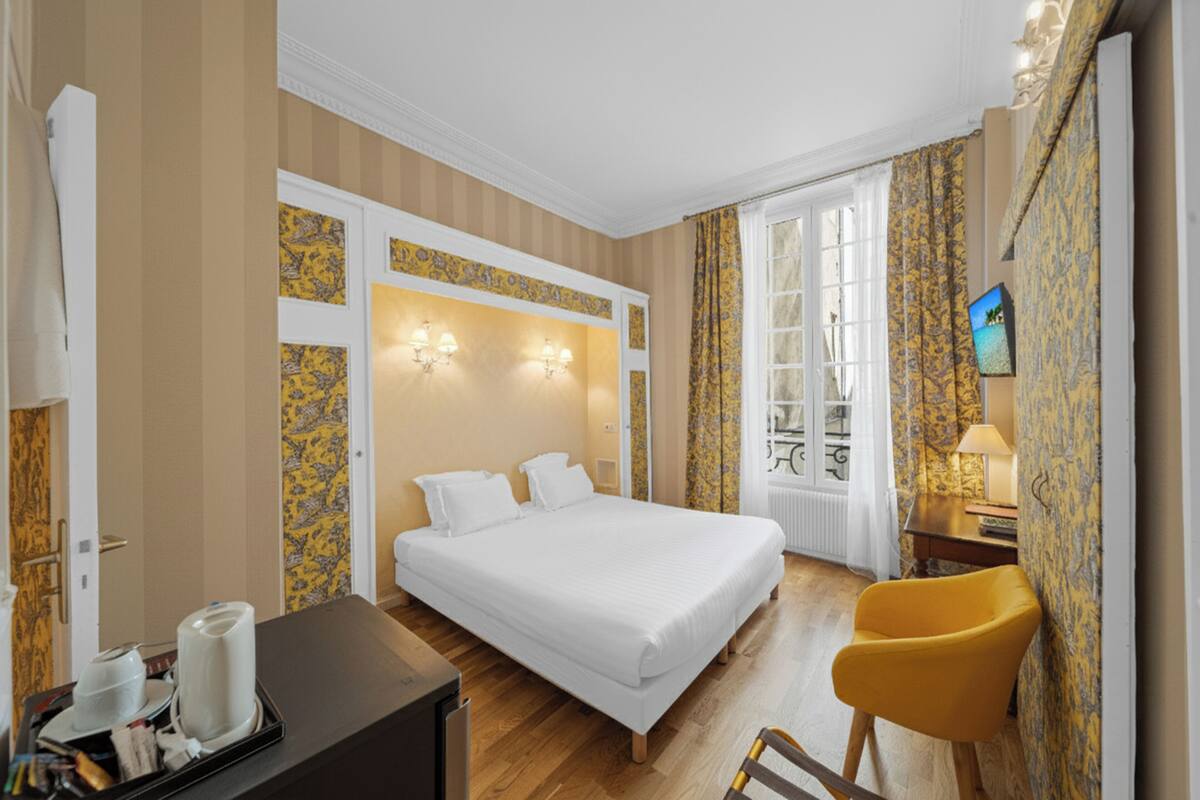 Quarto de hotel com uma cama grande, uma mesa com luminária, uma cadeira e uma televisão na parede.