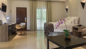 Quarto de hotel com cama, escrivaninha, cadeira, cafeteira e um vaso com flores.