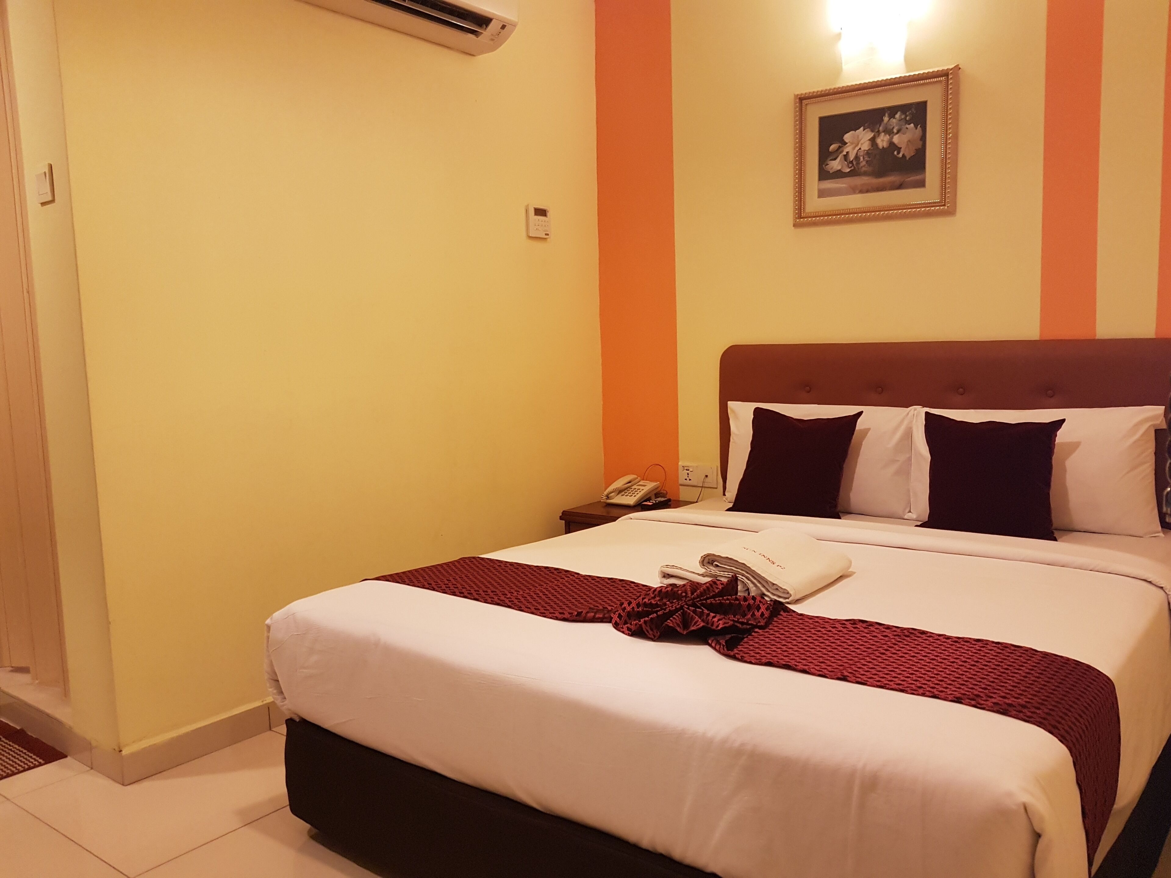 Quarto de hotel com cama, mesa de cabeceira, telefone e ar condicionado fixado na parede.
