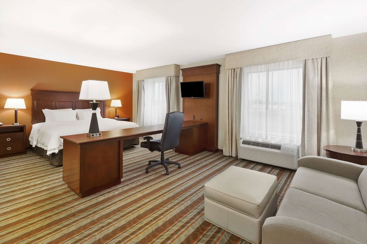 Quarto de hotel com cama, escrivaninha, cadeira e televisão.