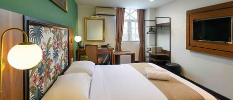 Quarto de hotel com cama, escrivaninha, cadeira, televisão e ar condicionado.