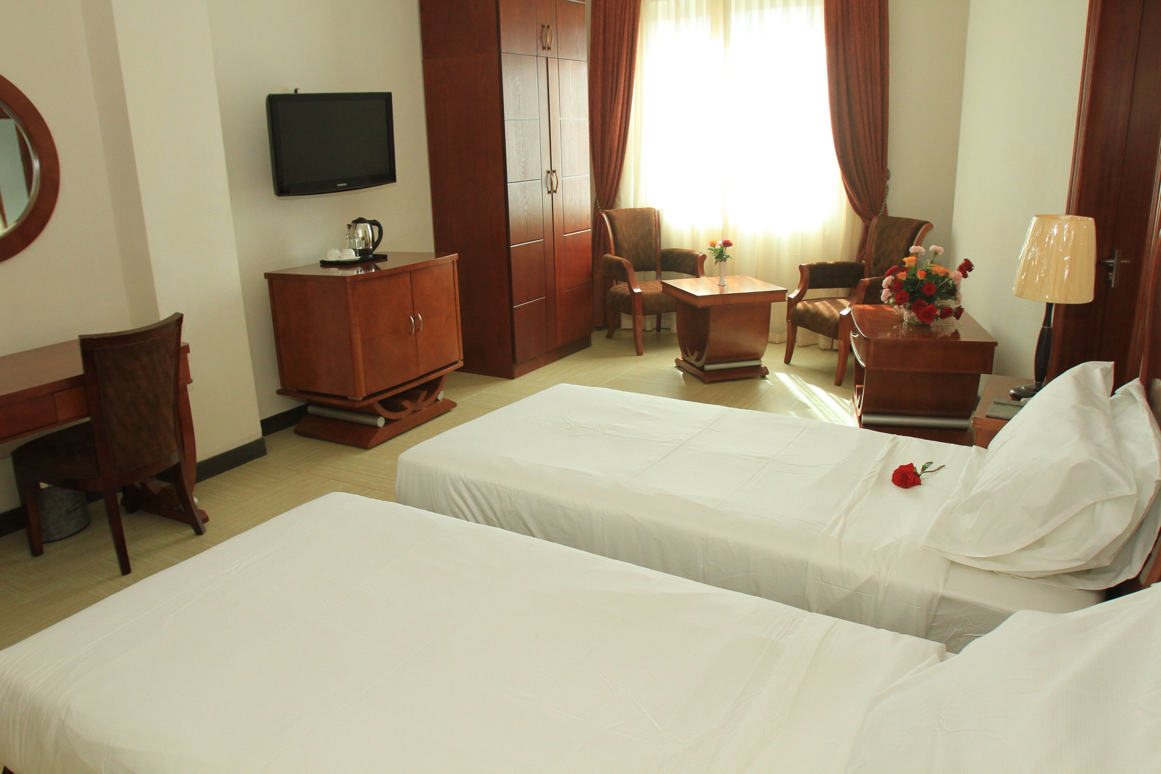 Quarto de hotel com duas camas, televisão, escrivaninha, cadeira e armário.